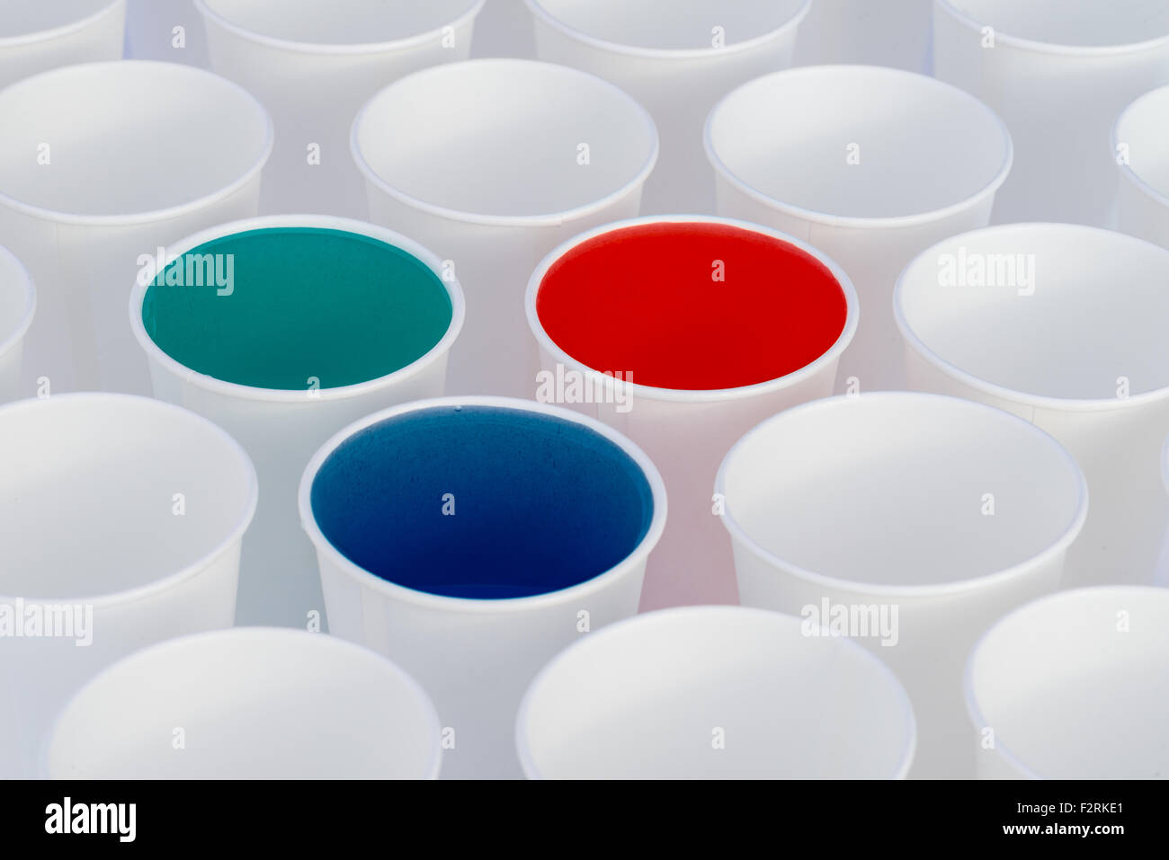 White paper cups on a white background. Some cups have colored liquid ...