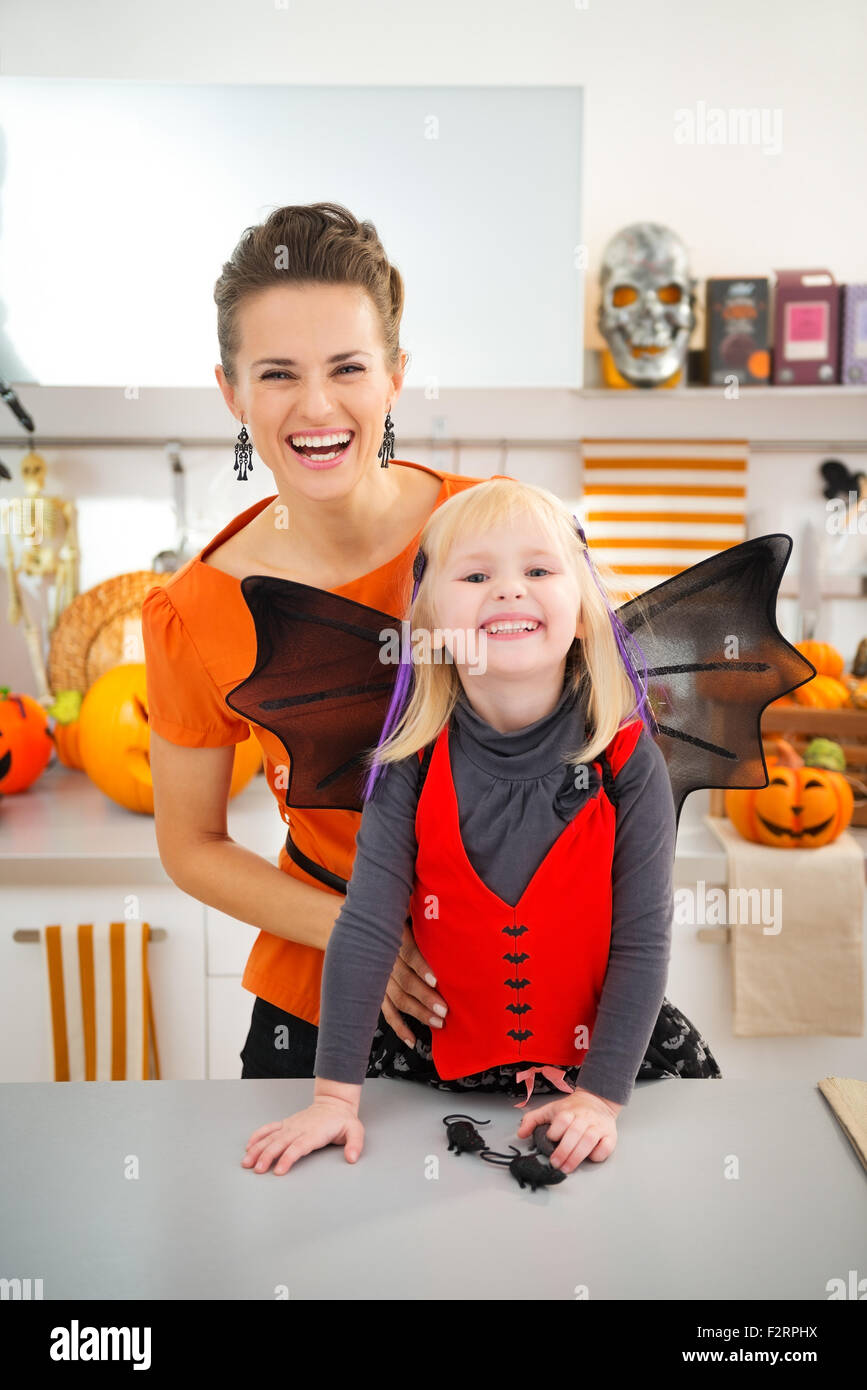 Funny blond girl in halloween bat costume with young mother preparing ...