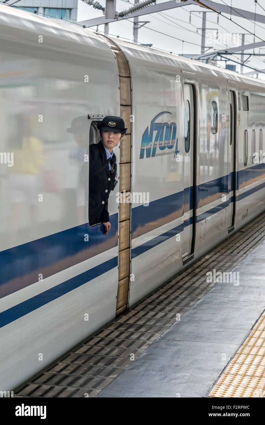 A guard on a Shinkansen bullet train leans out of the window of the ...