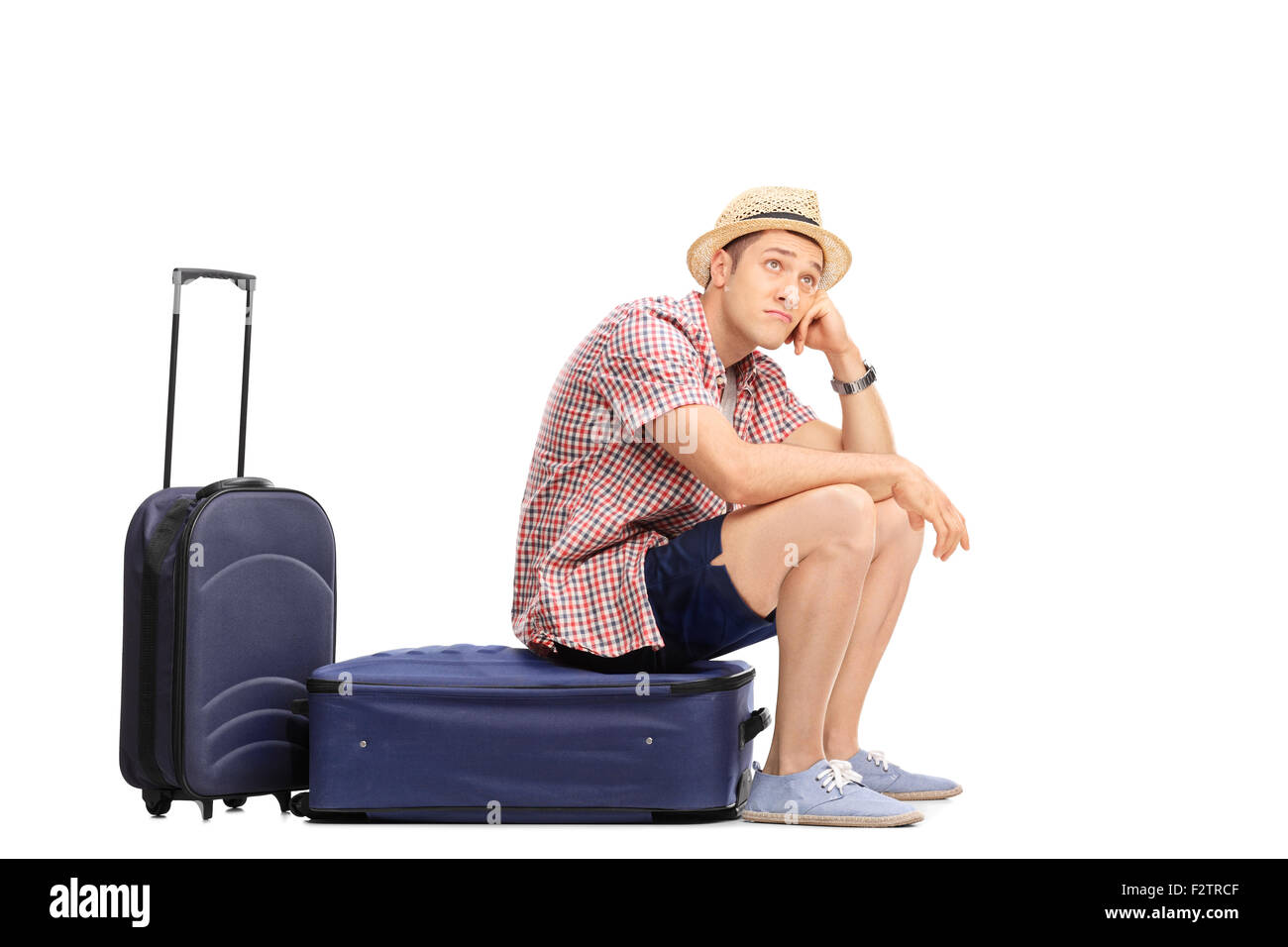 Bored male tourist sitting on his baggage and looking in the distance ...