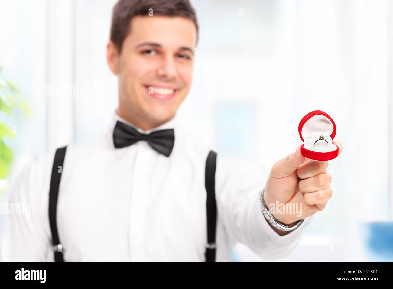 Elegant young man proposing with an engagement ring at home with the ...