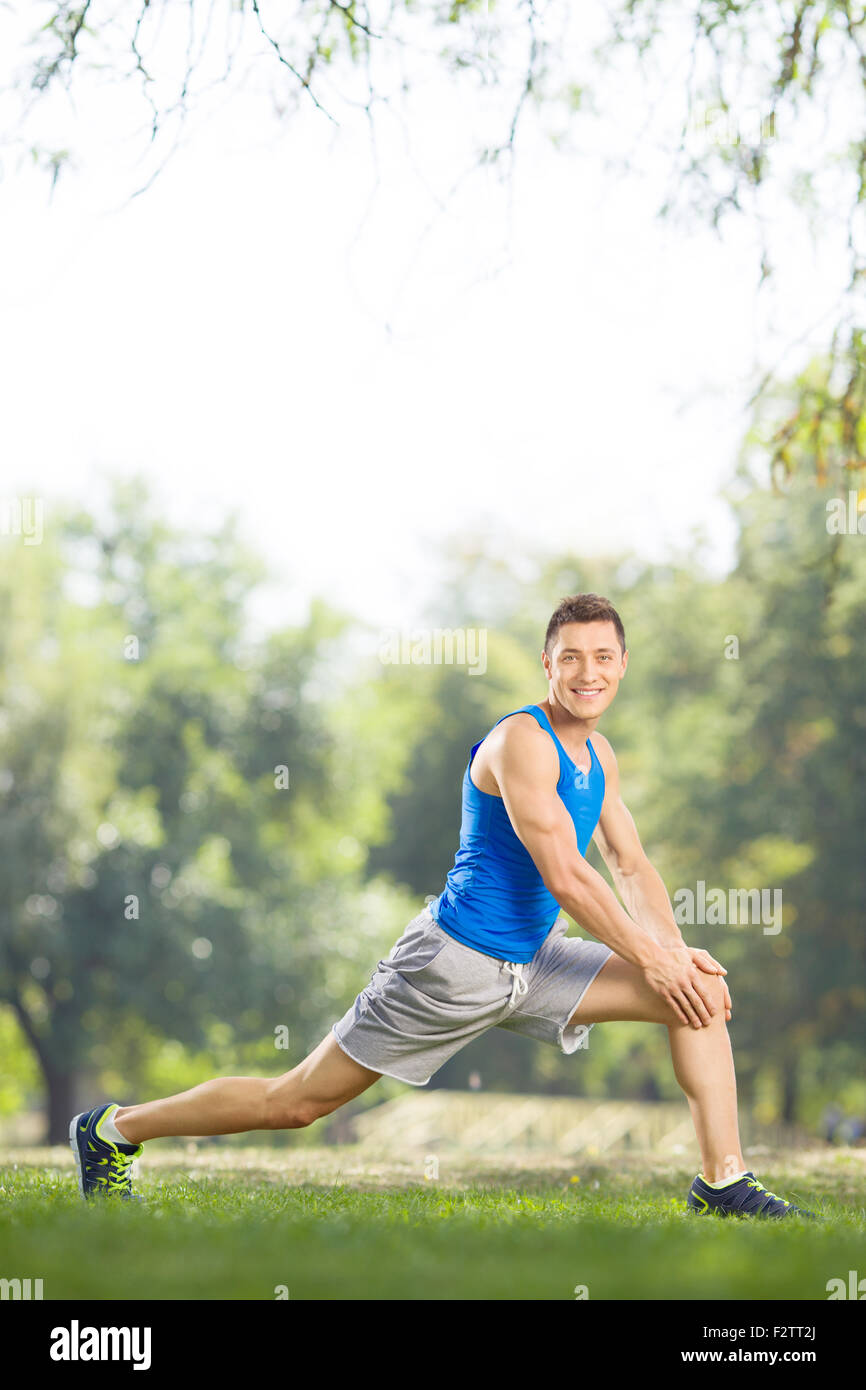 Vertical shot of a young athlete doing stretching exercises in a park ...