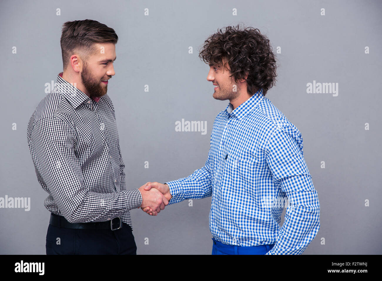 Portrait of a two casual men doing handshake over gray background Stock ...