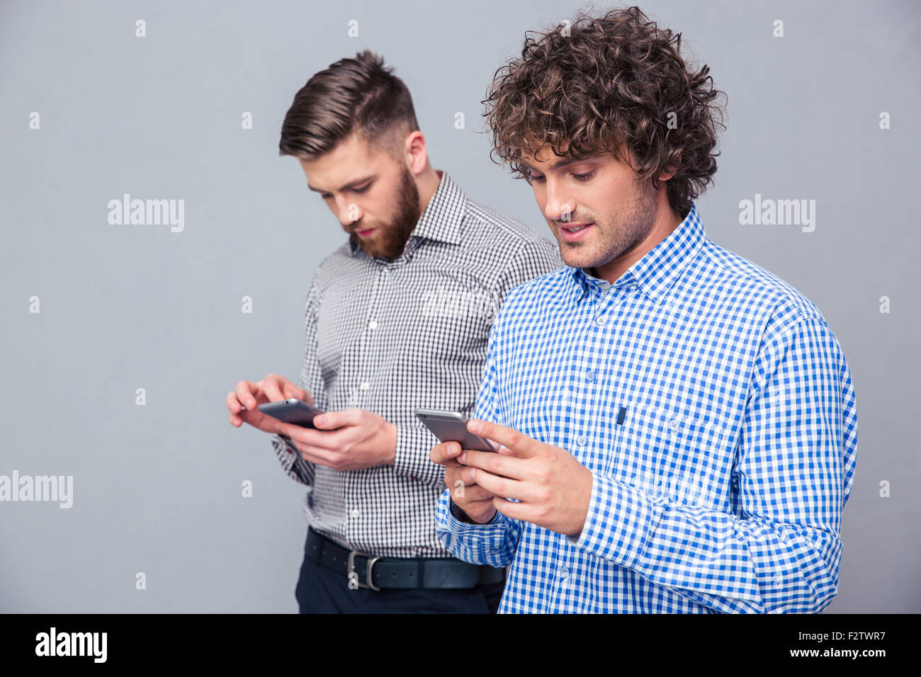 Portrait of a two serious men using smartphone over gray background ...