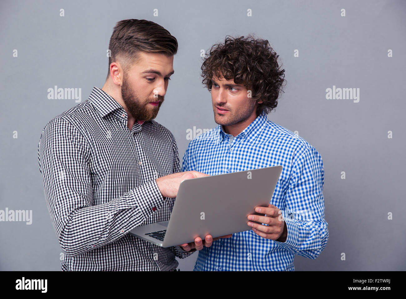 Portrait of a two men using laptop over gray background Stock Photo - Alamy