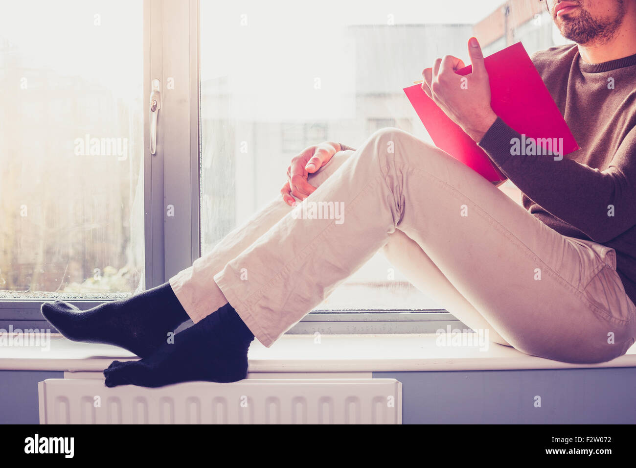 Young man is sitting on window sill and reading Stock Photo - Alamy
