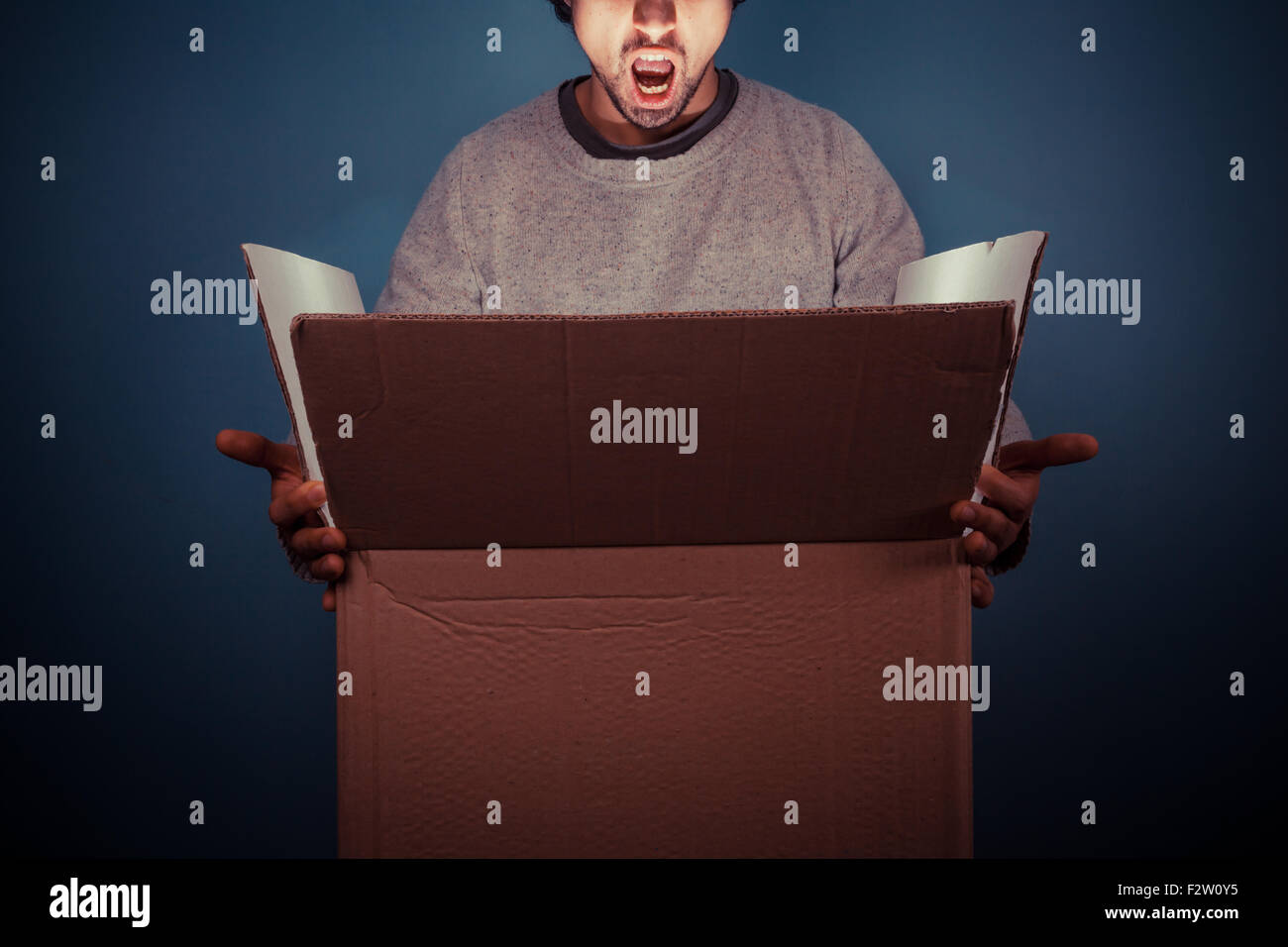 Surprised young man is opening a large cardboard box with something ...