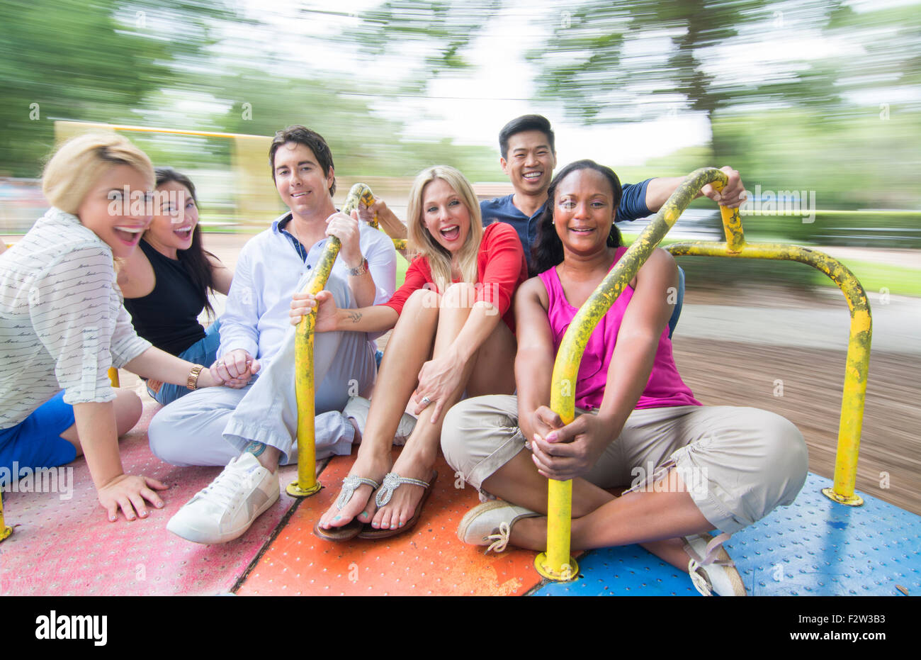mixed ethnic friends spinning on merry go round in playground laughing ...