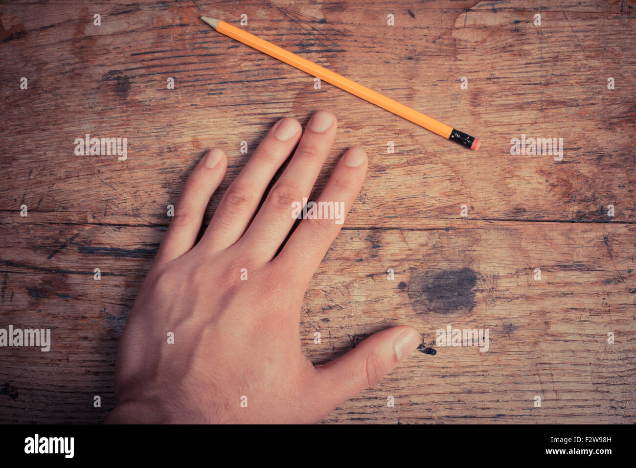 Hand resting on a table with a pencil next to it Stock Photo - Alamy