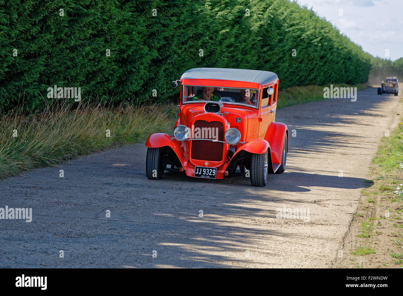 A couple in an orange early Ford American classic car lowered hot rod ...