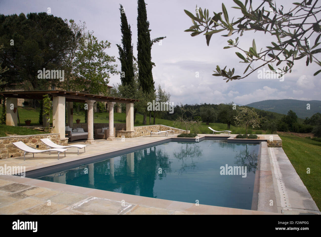 White loungers beside swimming pool and covered veranda in garden of ...