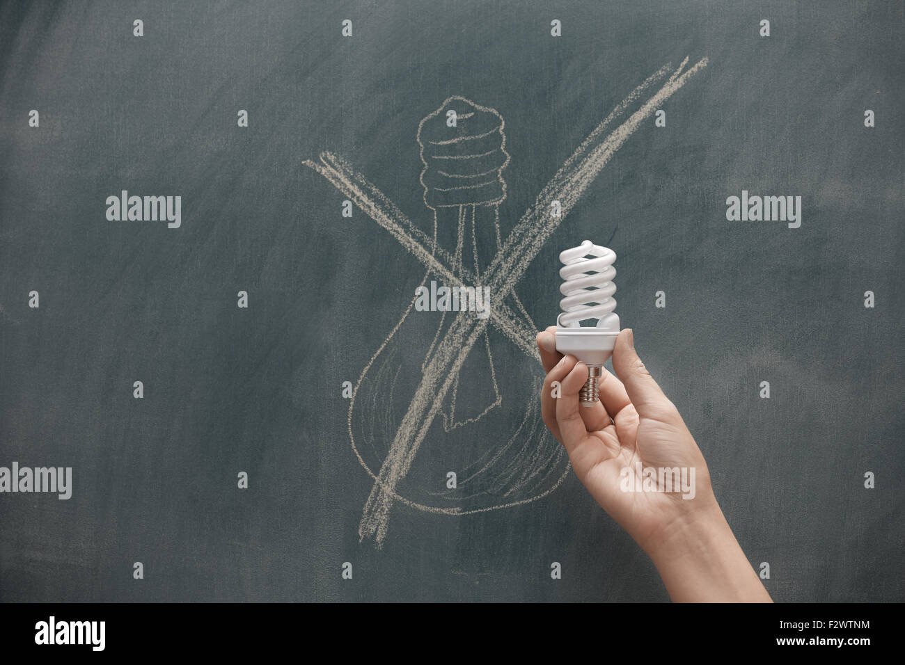 Human hand holding energy saving lamp at the blackboard with ...