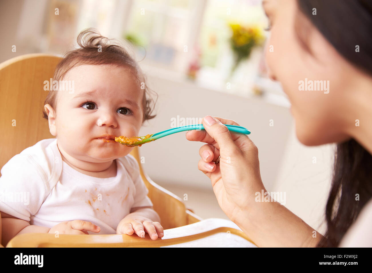 Happy Baby Being Fed In High Chair At Meal Time Stock Photo - Alamy