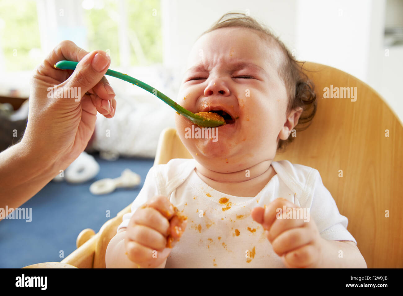 Unhappy Baby Being Fed In High Chair At Meal Time Stock Photo - Alamy