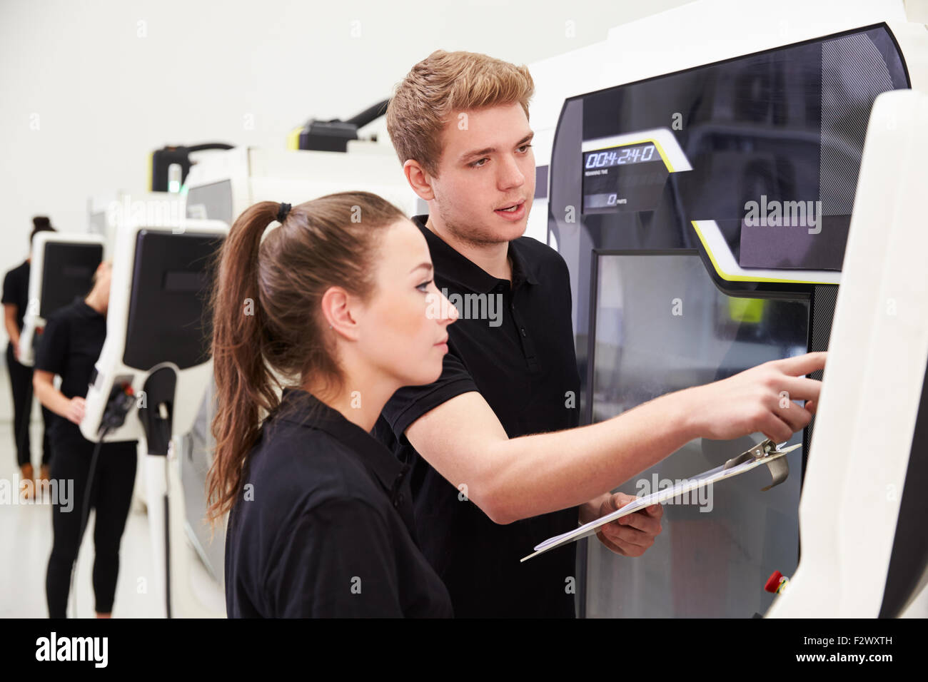 Two Young Engineers Operating CNC Machinery On Factory Floor Stock ...