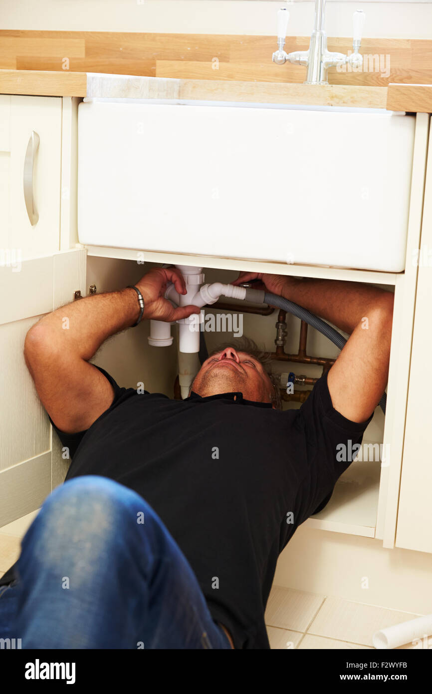 A plumber lying on his back to fix a kitchen sink, vertical Stock Photo ...