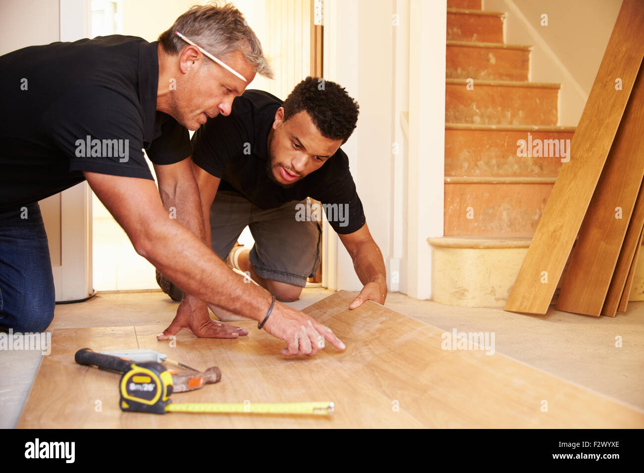 Two men laying wood panel flooring in a house Stock Photo - Alamy