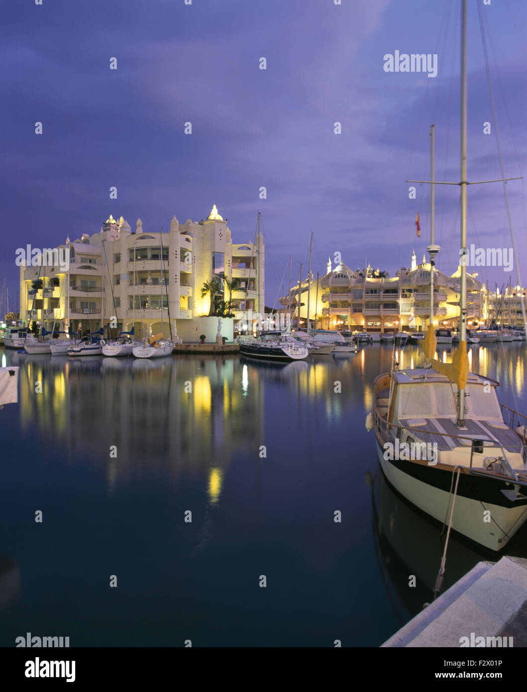 Boats in a Spanish marina lit with apartment buildings lit at night ...