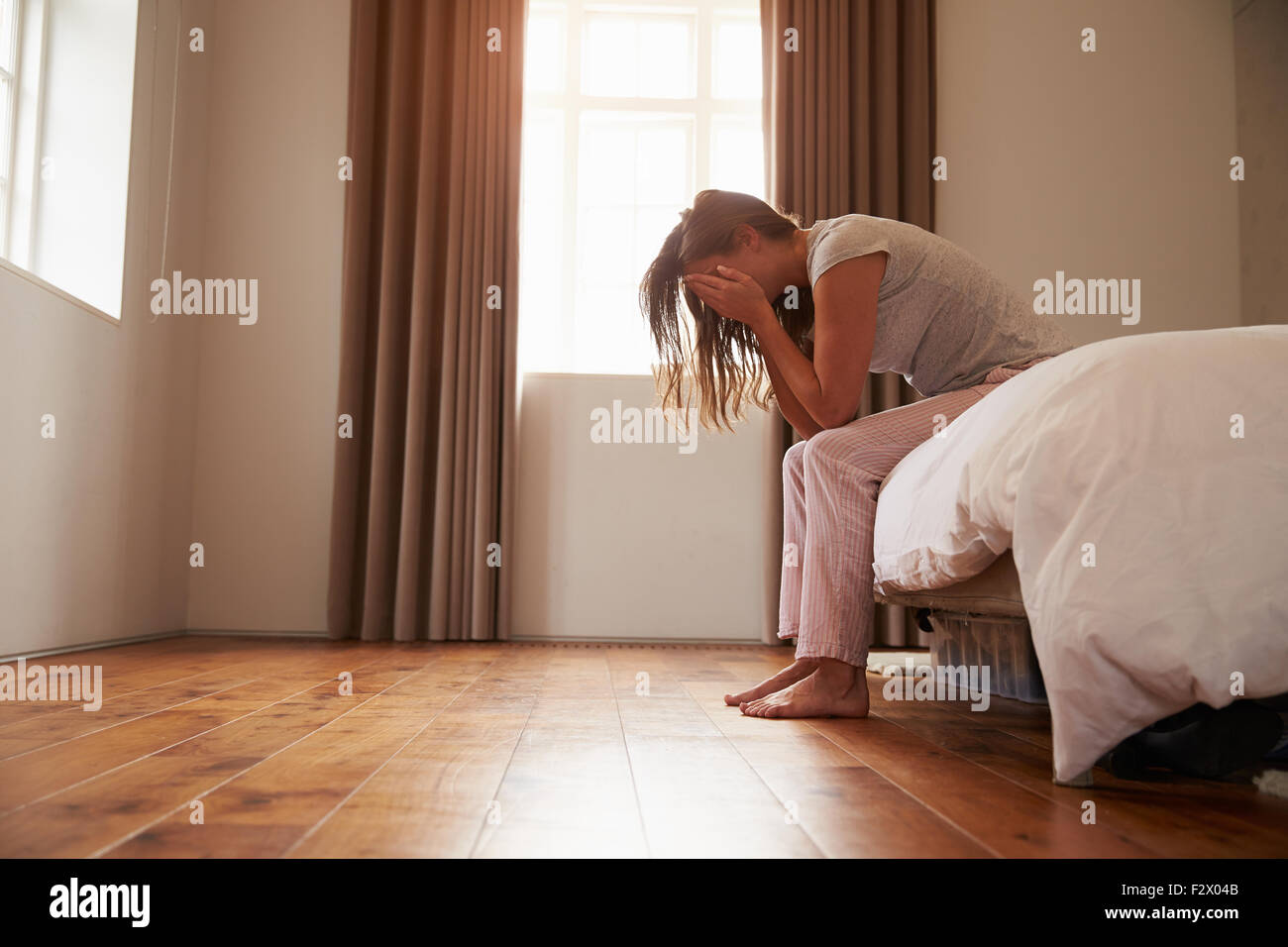 Woman Suffering From Depression Sitting On Bed In Pajamas Stock Photo ...