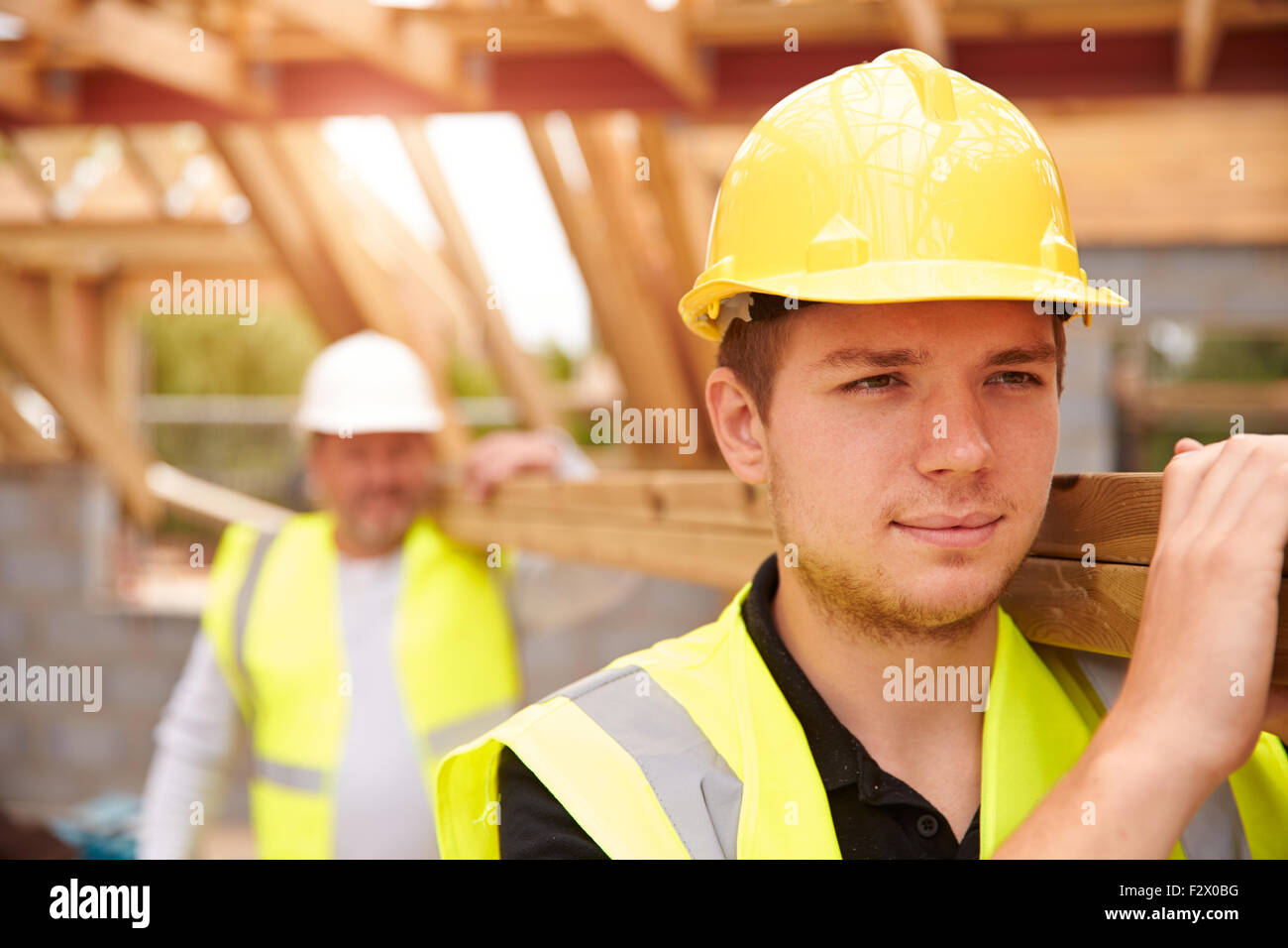 Builder And Apprentice Carrying Wood On Construction Site Stock Photo ...