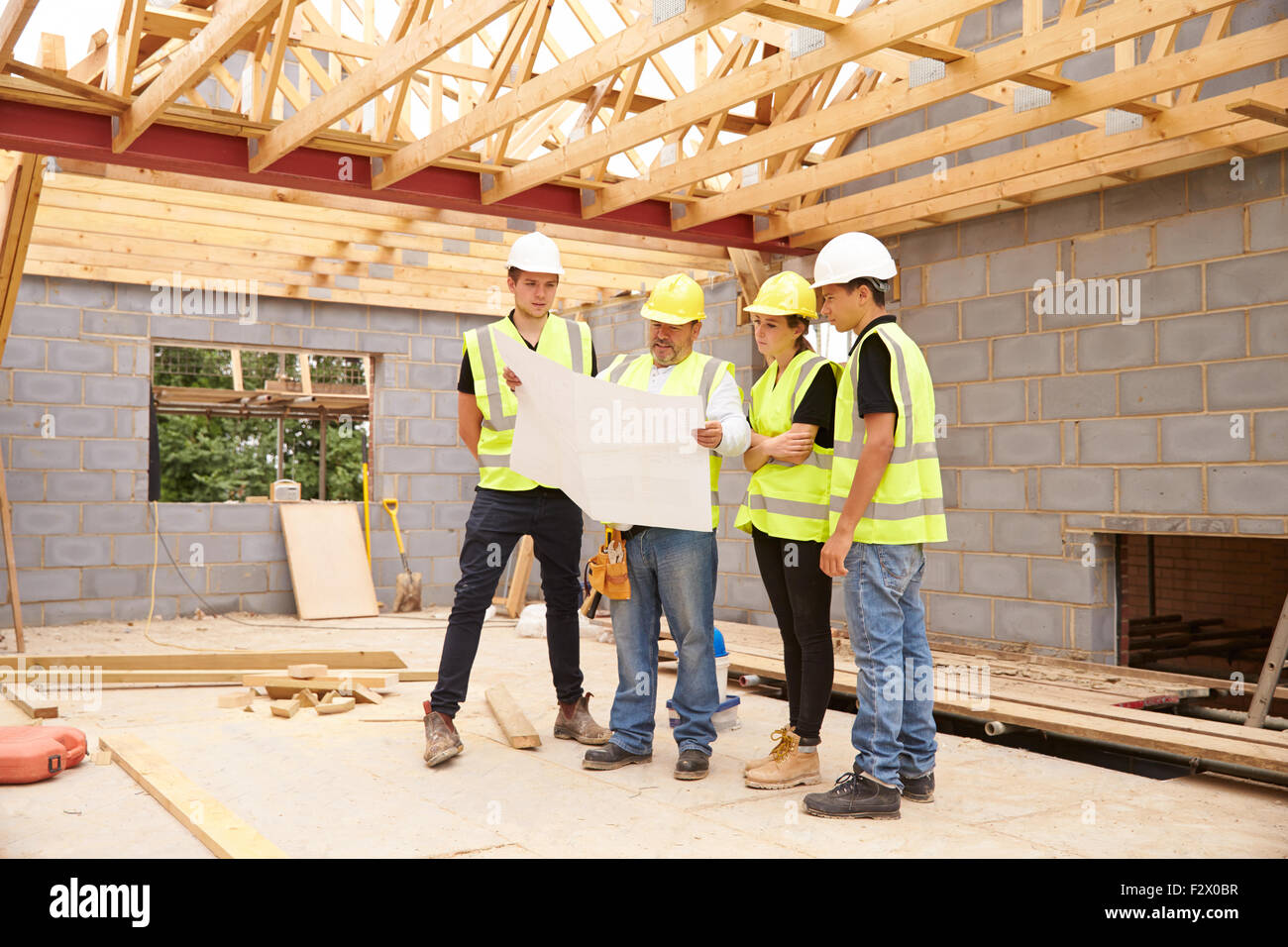 Builder On Building Site Looking At Plans With Apprentices Stock Photo ...