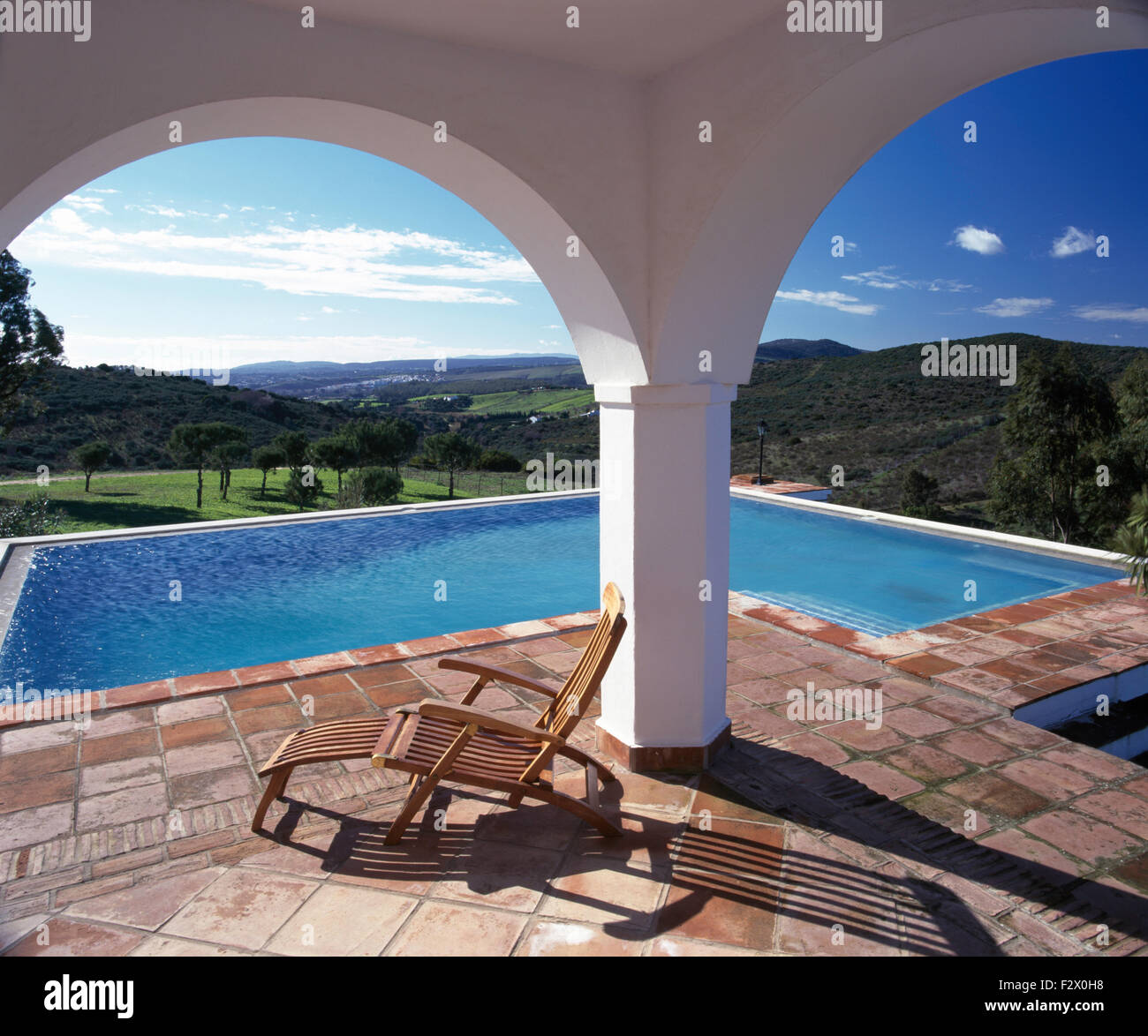Wooden lounger on veranda of Spanish villa with a view of swimming pool ...