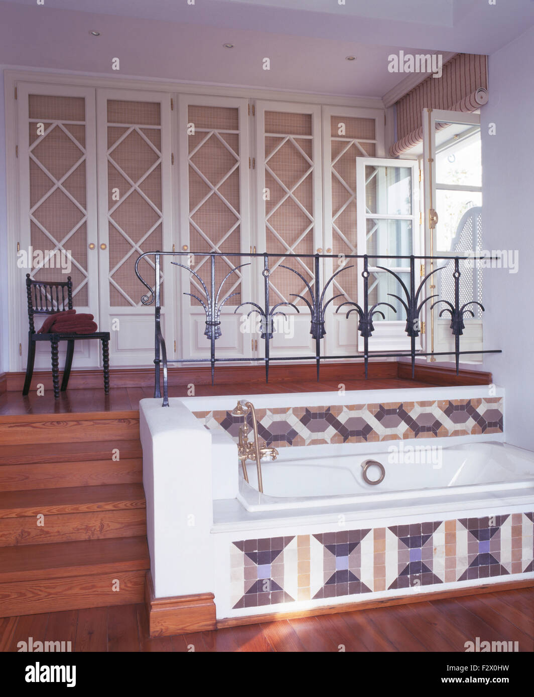 Tiled surround and splash back on bath in modern bathroom with steps up ...