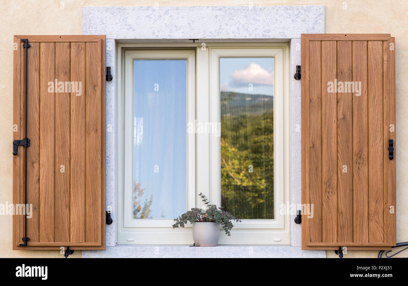 a nice window with open brown wooden shutters and flowers in the pot ...