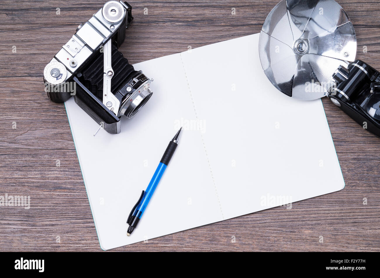Image shows a notepad with pen and, flashlight and camera on a wooden ...