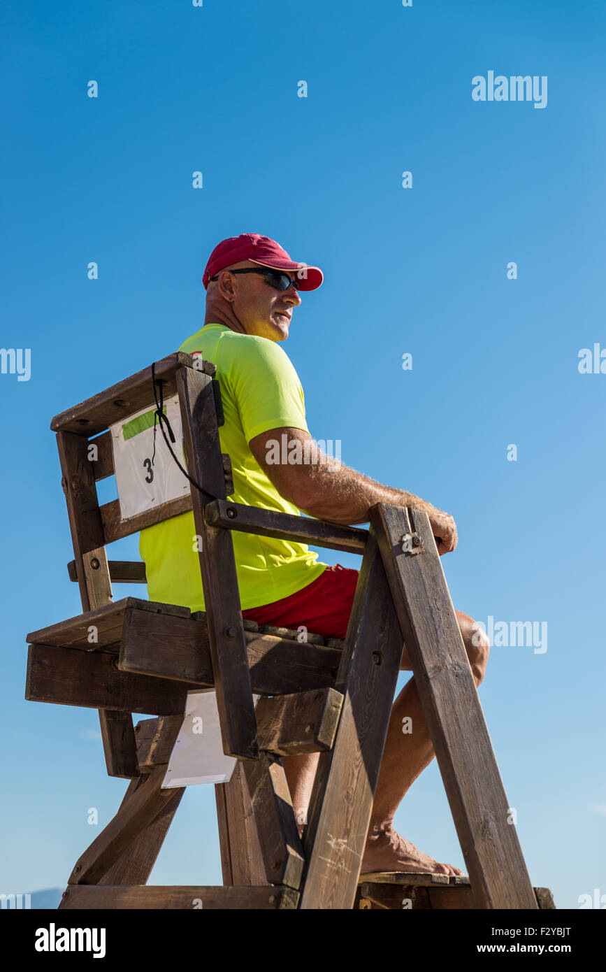 Lifeguard sitting high up on his chair watching the beach Stock Photo ...