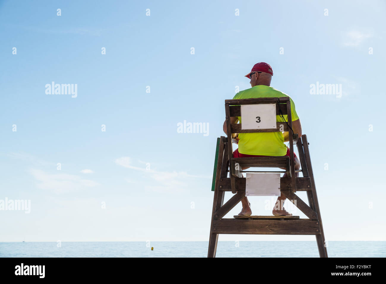 Lifeguard sitting high up on his chair watching the beach Stock Photo ...