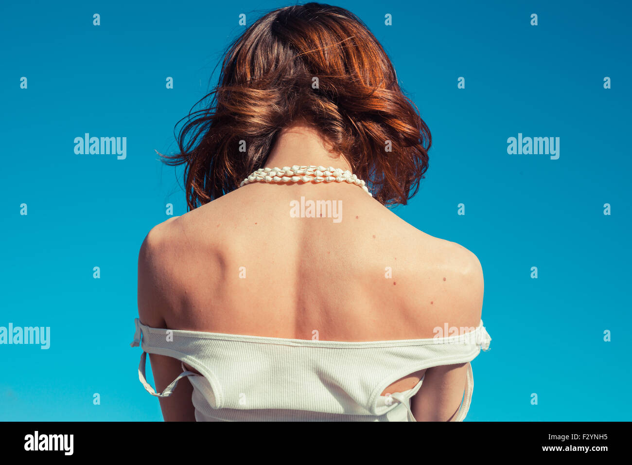A young woman is tanning her back on a sunny day with a clear blue sky ...