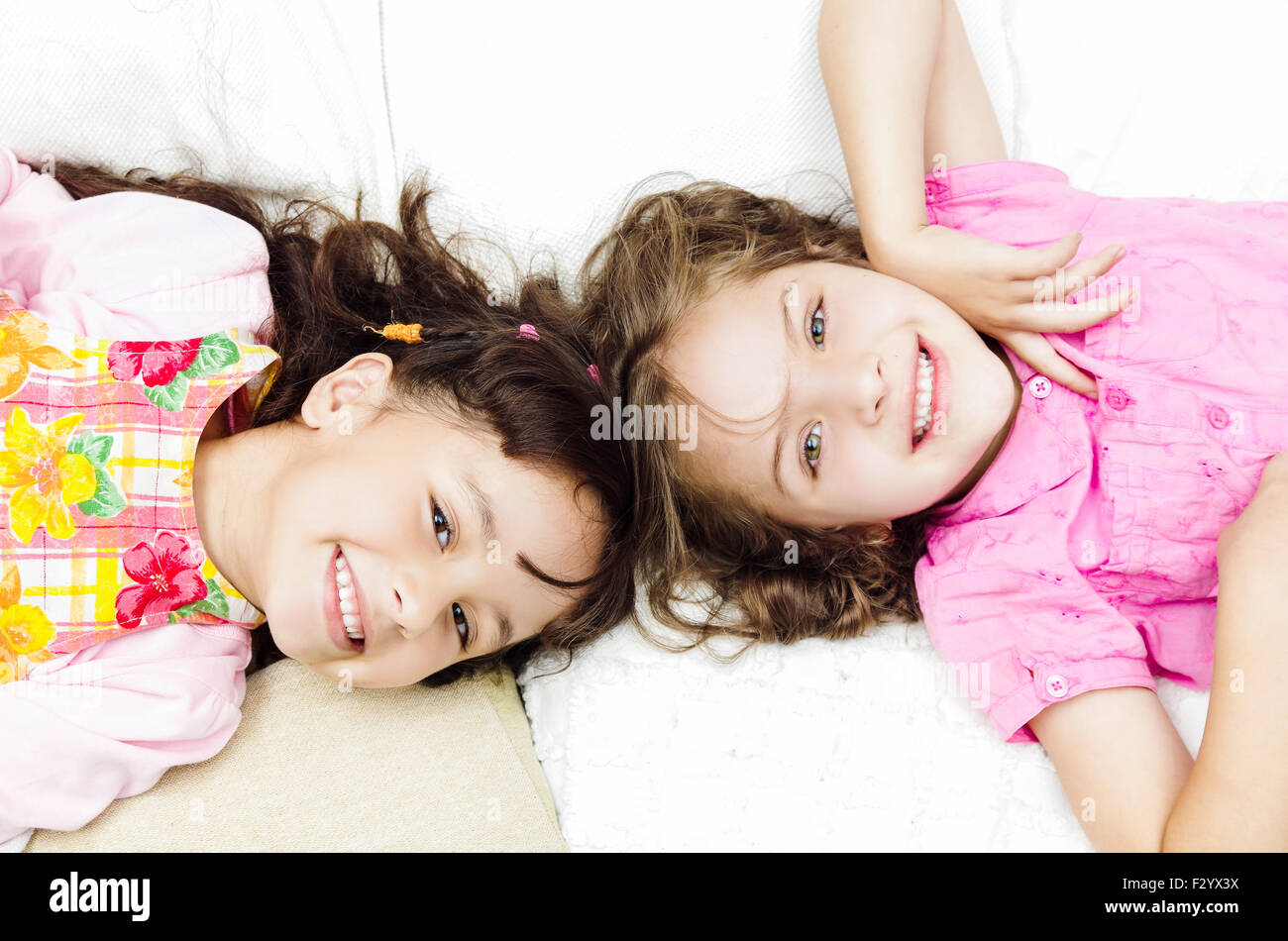 Young adorable hispanic sisters lying down playing and embracing each ...