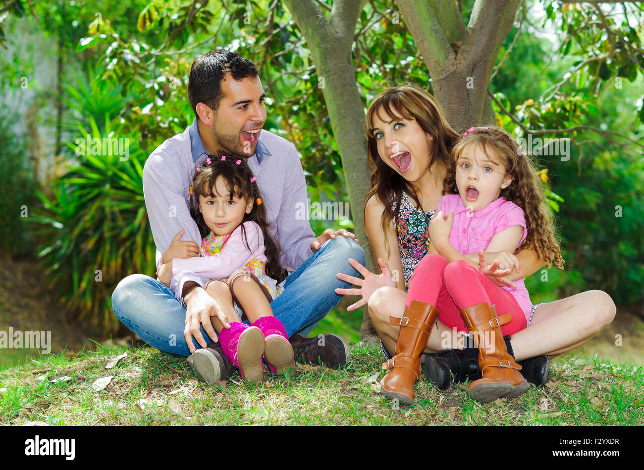 Beautiful hispanic family of four sitting outside on grass engaging in ...