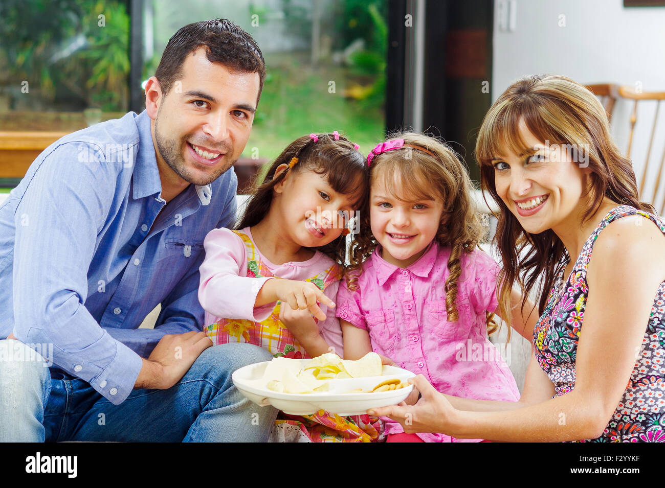 Hispanic parents with two daughters eating from a tray of potato chips ...