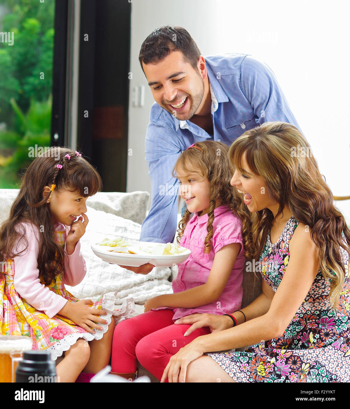 Hispanic parents with two daughters eating from a tray of potato chips ...