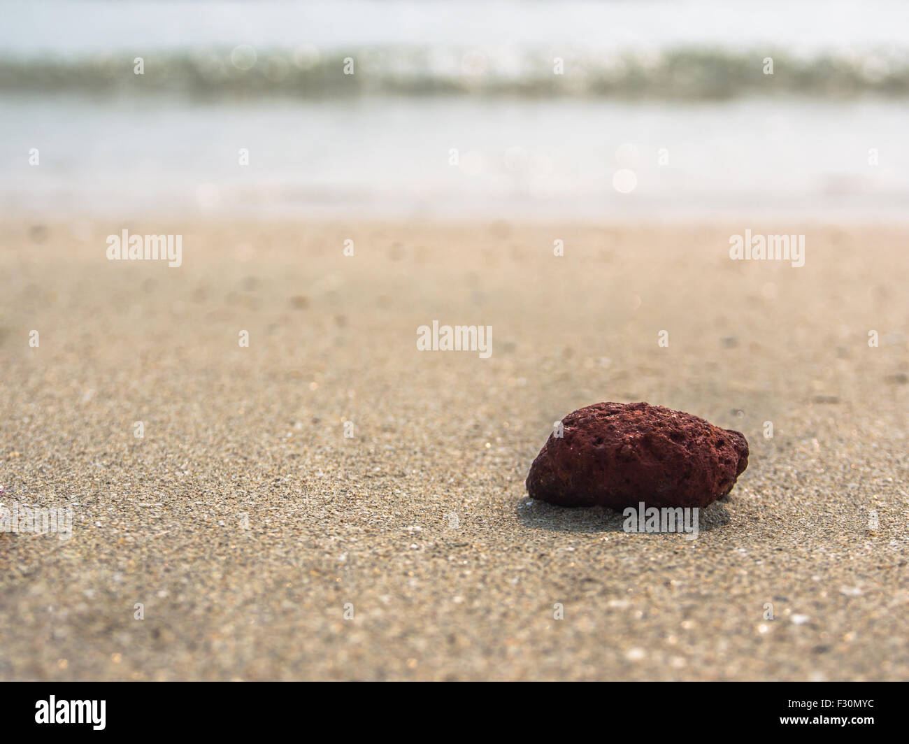 Red rock on the beach with blur sea background Stock Photo - Alamy