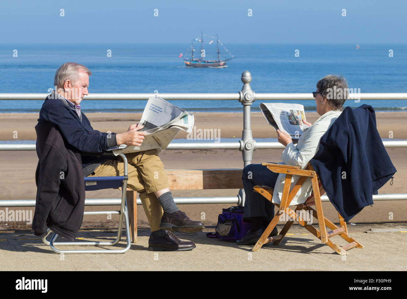 Elderly couple reading newspapers overlooking beach at Whitby, North ...