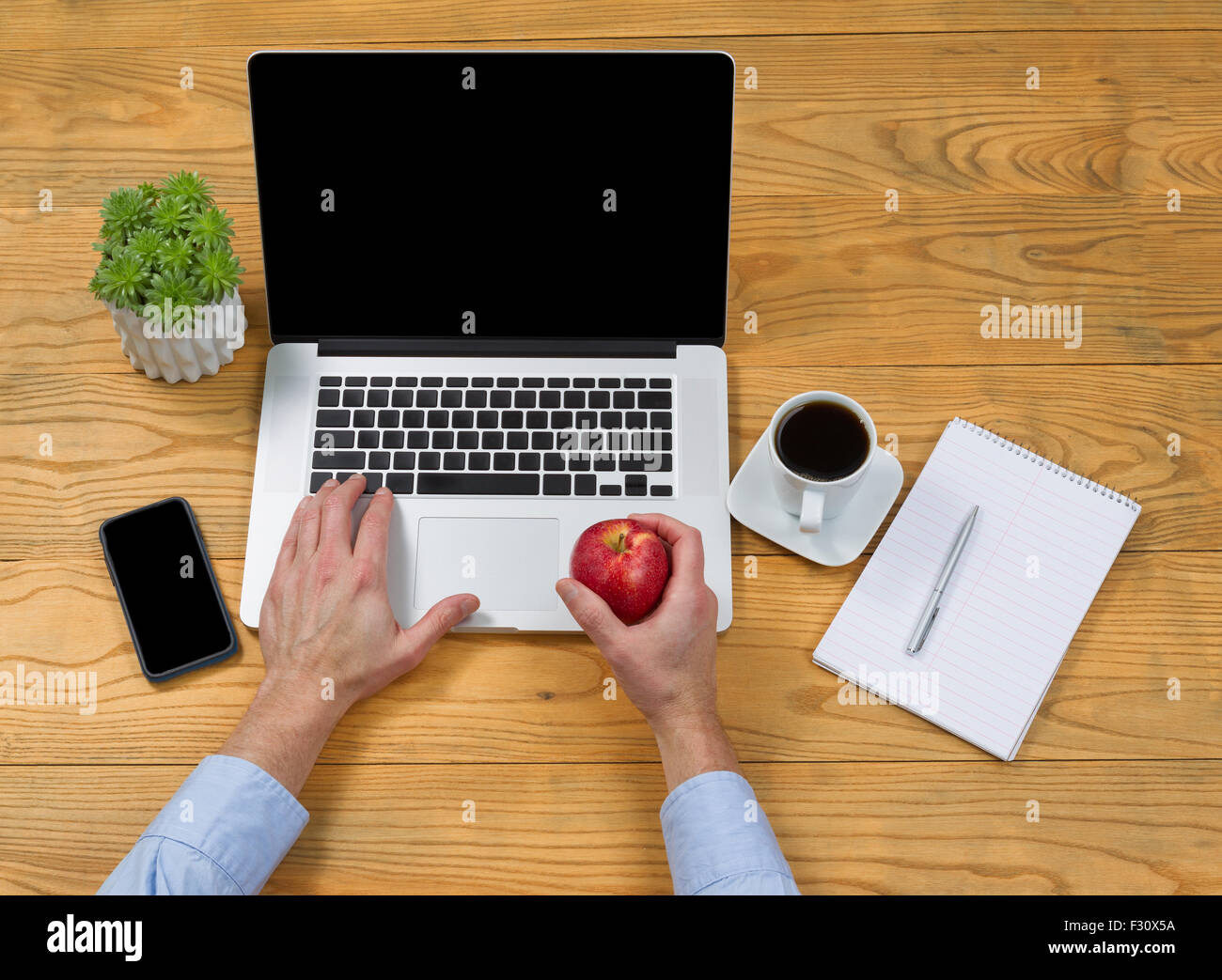 High angled view of male hand holding apple while typing on computer ...