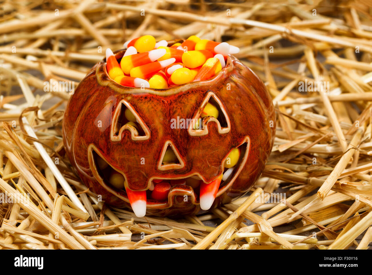 Front view of scary pumpkin with fangs filled with candy corn on straw ...