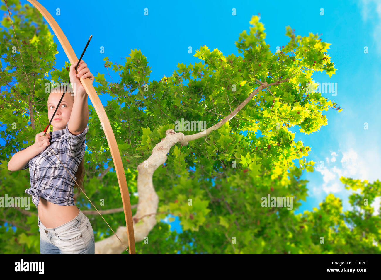 Teen girl practicing archery with green tree in background Stock Photo ...