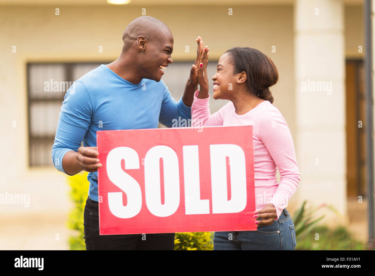 cheerful young African couple holding sold sign and celebrating their ...