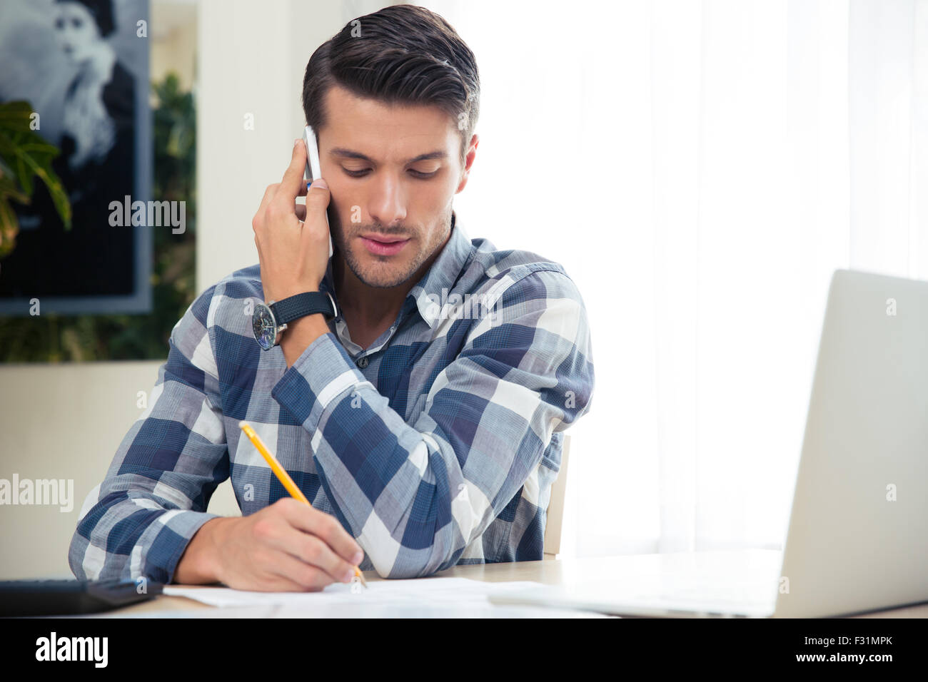 Portrait of a man making notes on the bills while talking on the phone ...