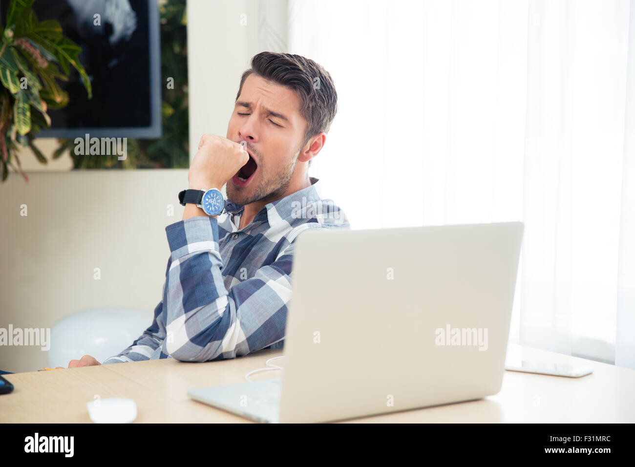 Portrait of a bored man yawning at the table with laptop at home Stock ...