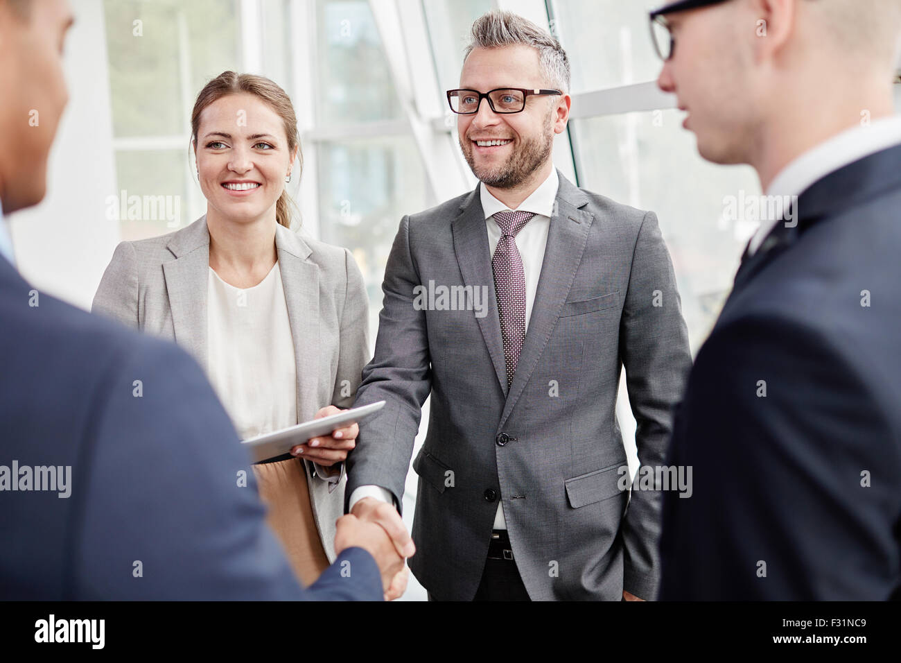 Happy colleagues looking at their business partner while greeting him ...