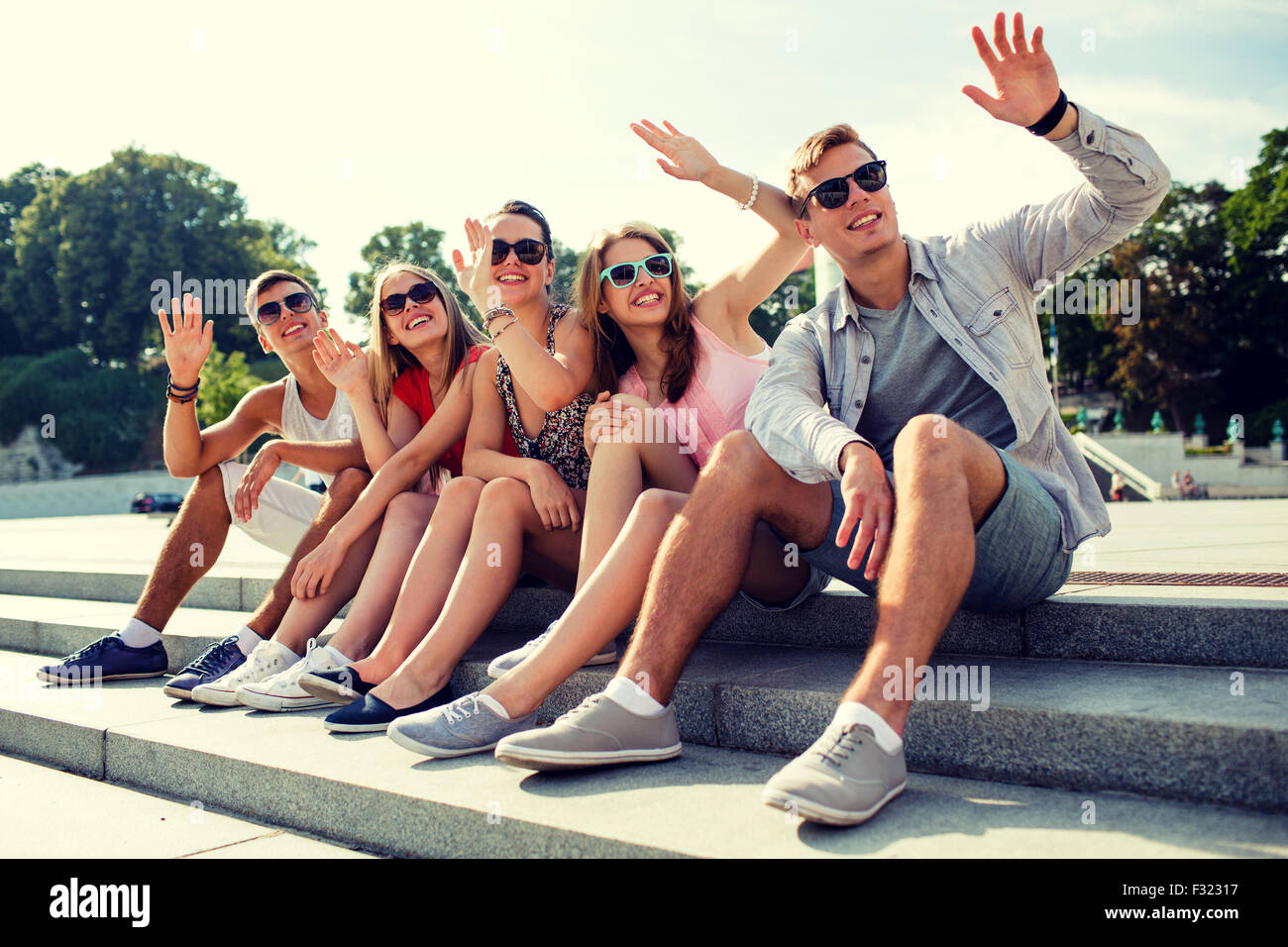 group of smiling friends sitting on city street Stock Photo - Alamy