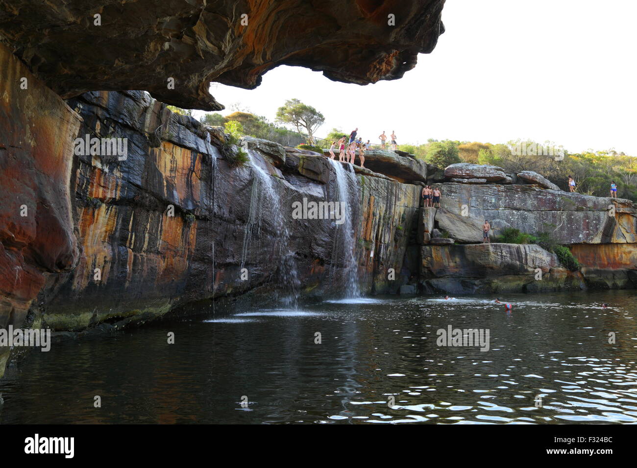 A crowd watches as cliff jumpers surface after jumping off cliff into a ...