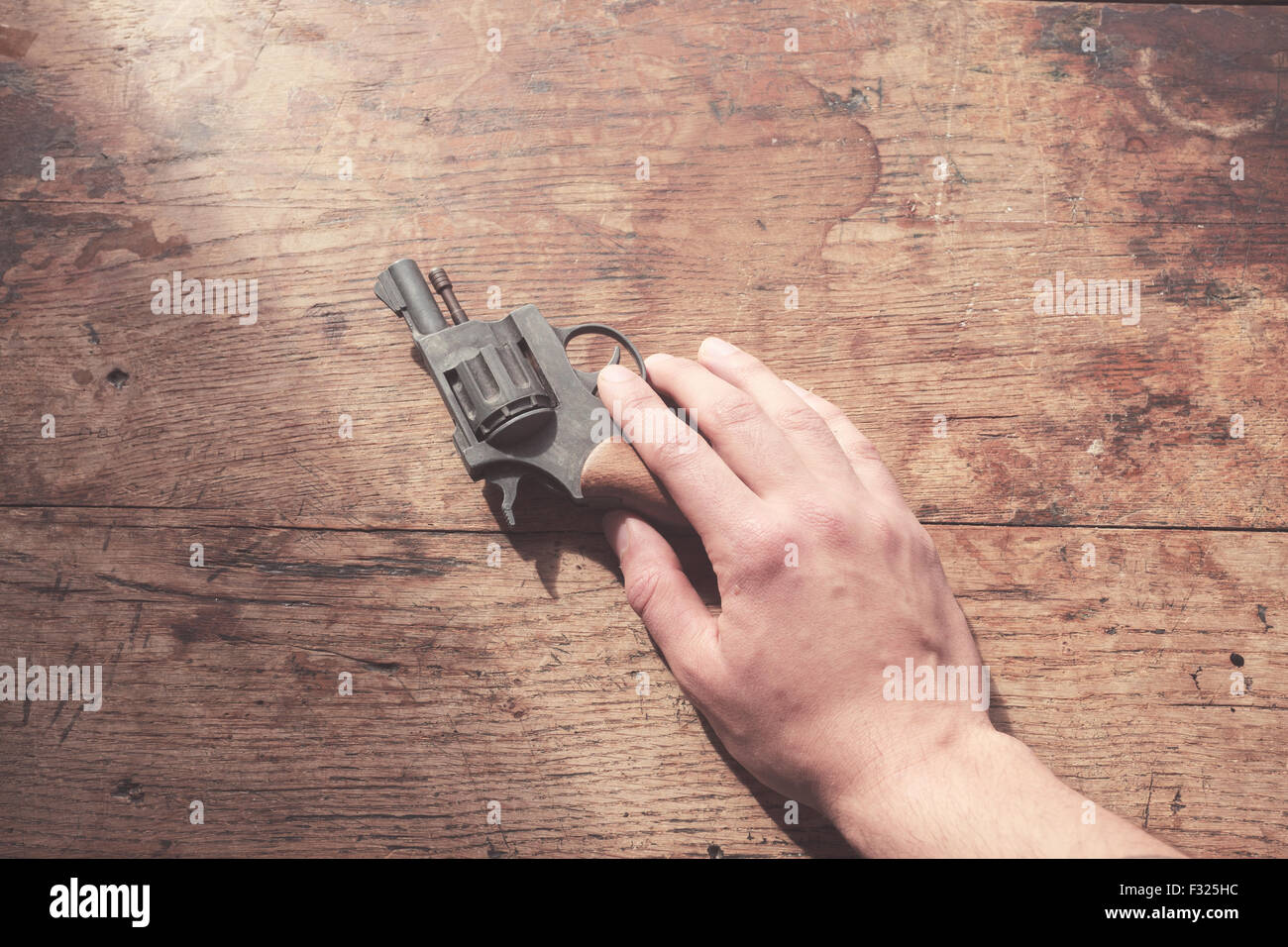 The hand of a man is holding a gun at a wood table Stock Photo - Alamy