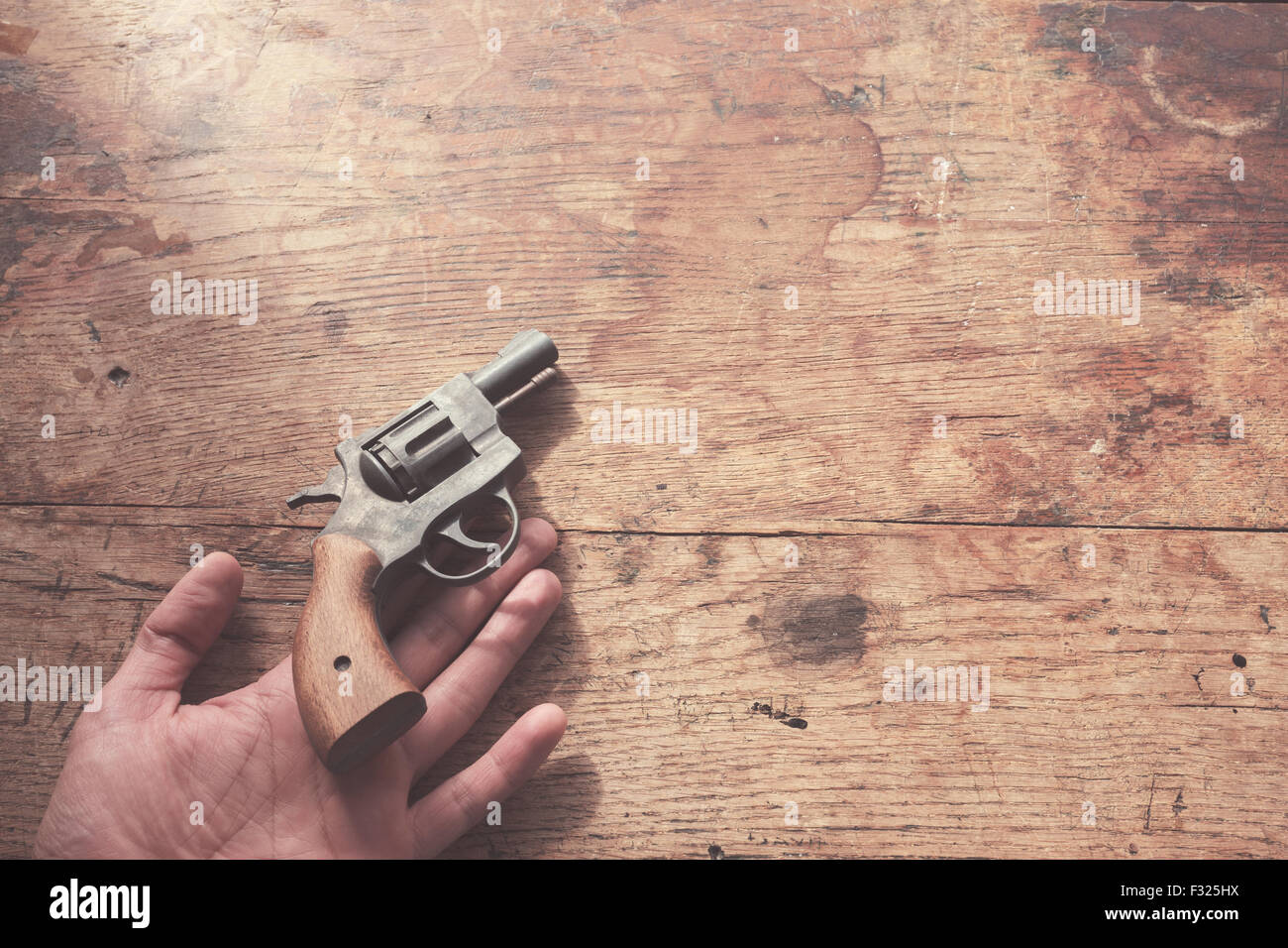 The hand of a man is holding a gun at a wood table Stock Photo - Alamy