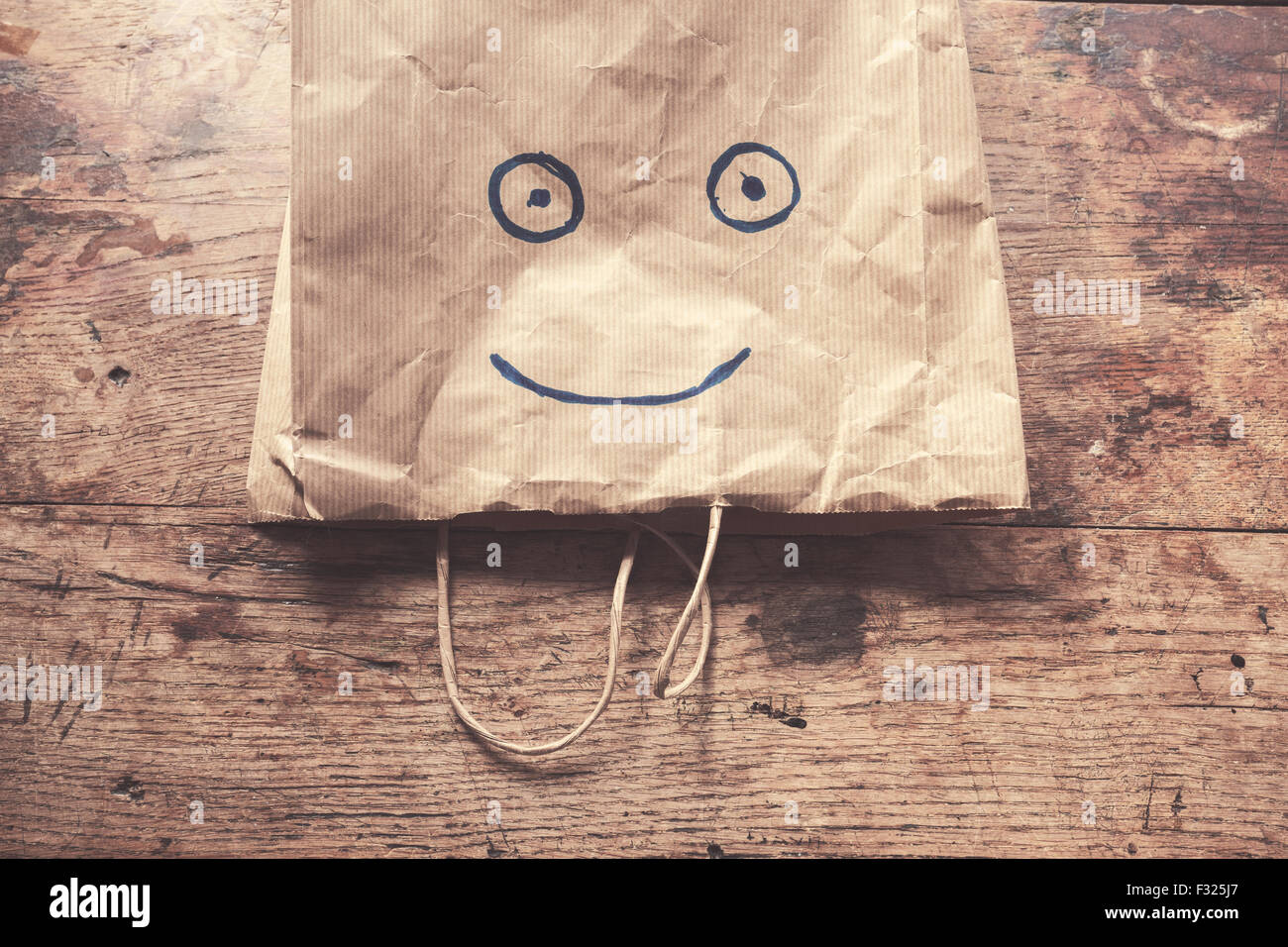 A paperbag with a smiling face painted on it lying on a wood table ...